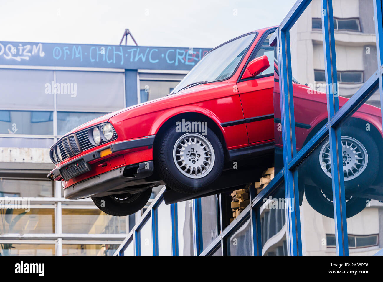 A red BMW car hangs precariously off the roof of a building, as if it ...
