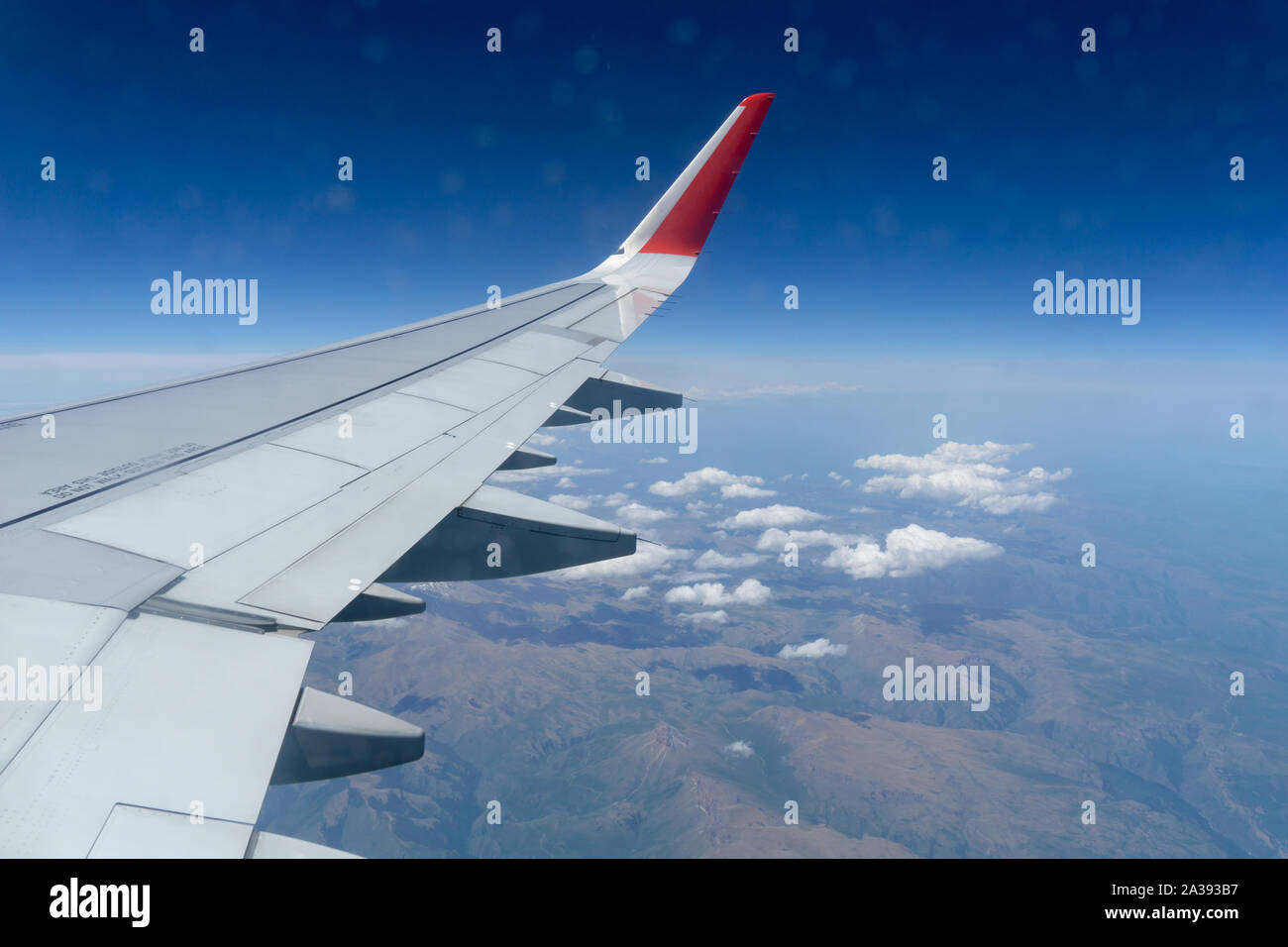 Wing of an airplane flying above the clouds over mountains Stock Photo ...