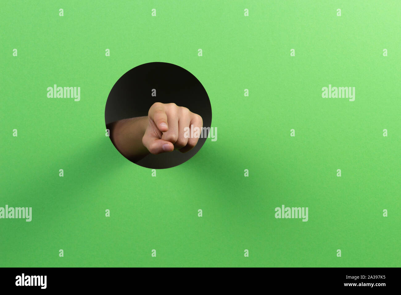 Hand through hole in light green background pointing with finger to ...