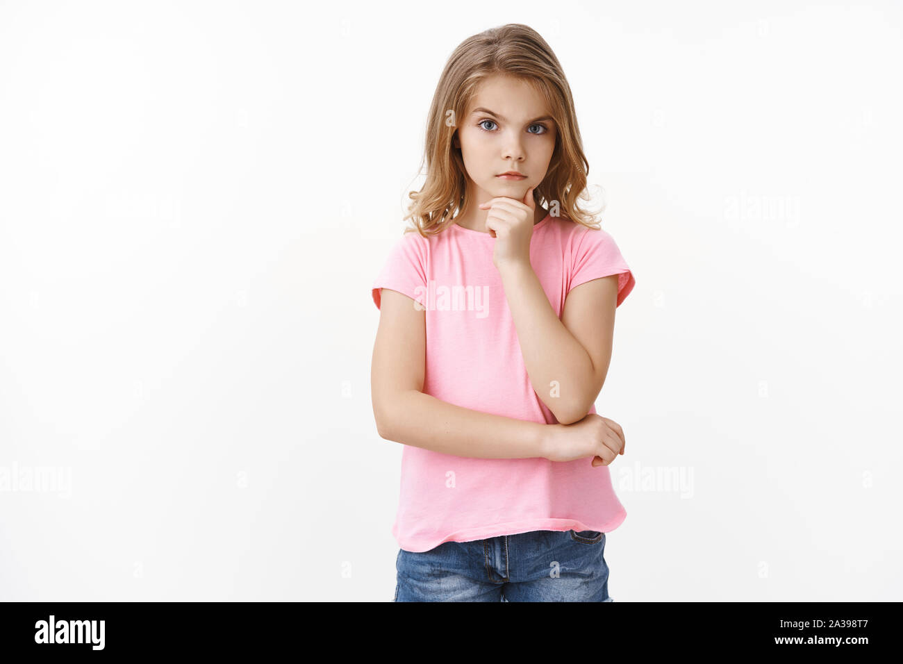 Serious-looking strict young little kid girl, touch chin frowning stare ...