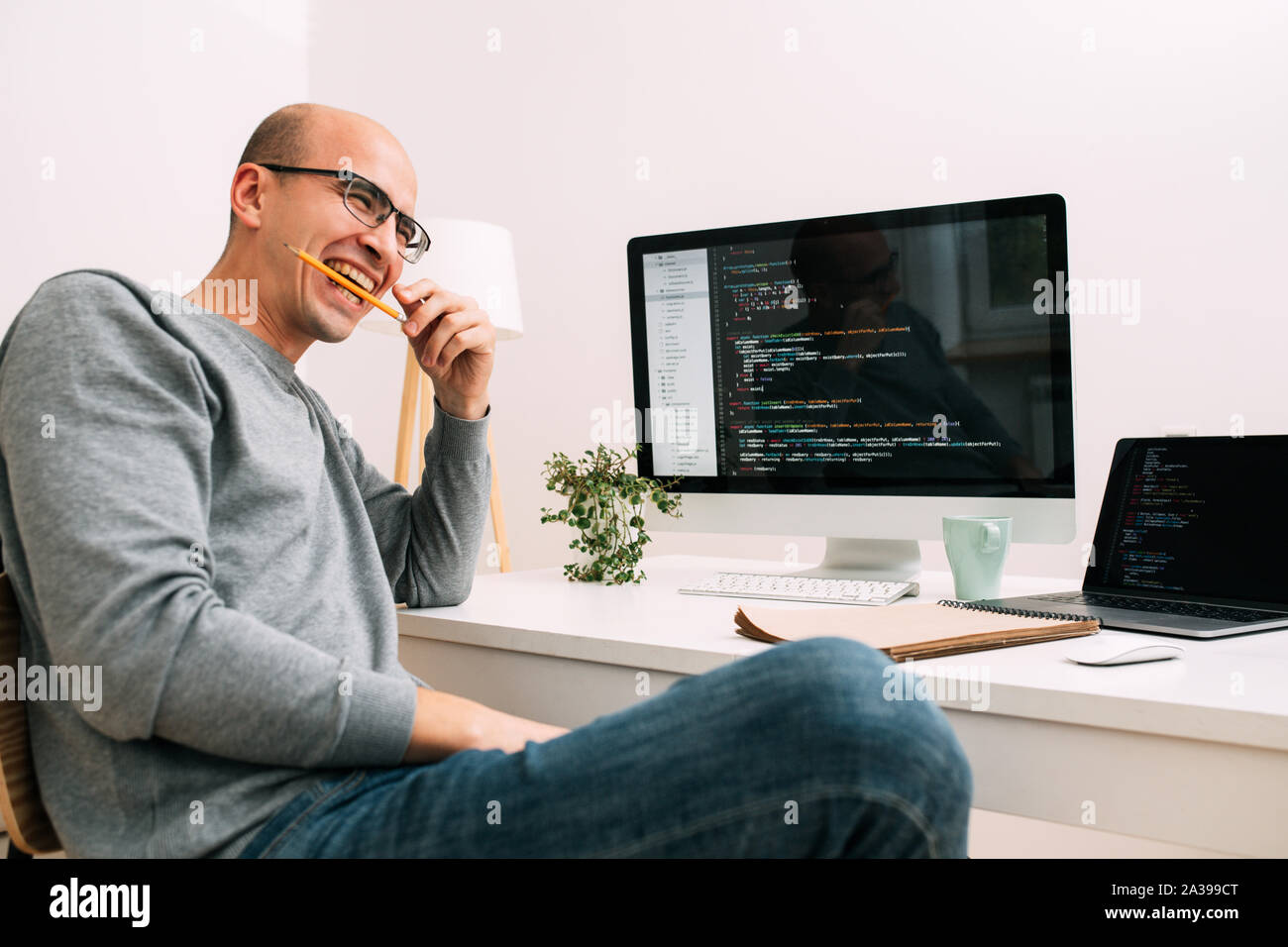 Programmer Working Behind The Desk With Two Screens Filled With Code