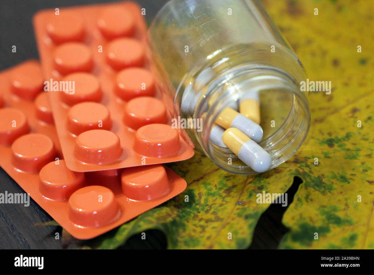 Pills on yellow maple leaf and dark wooden table, bottle of capsules ...