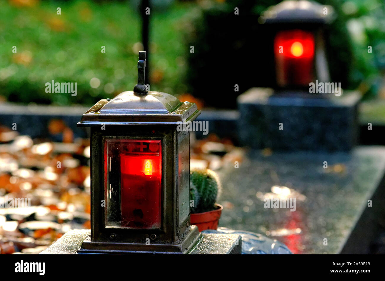 old metal grave lights with burning candles on a grave with autumn leaves in the background ...