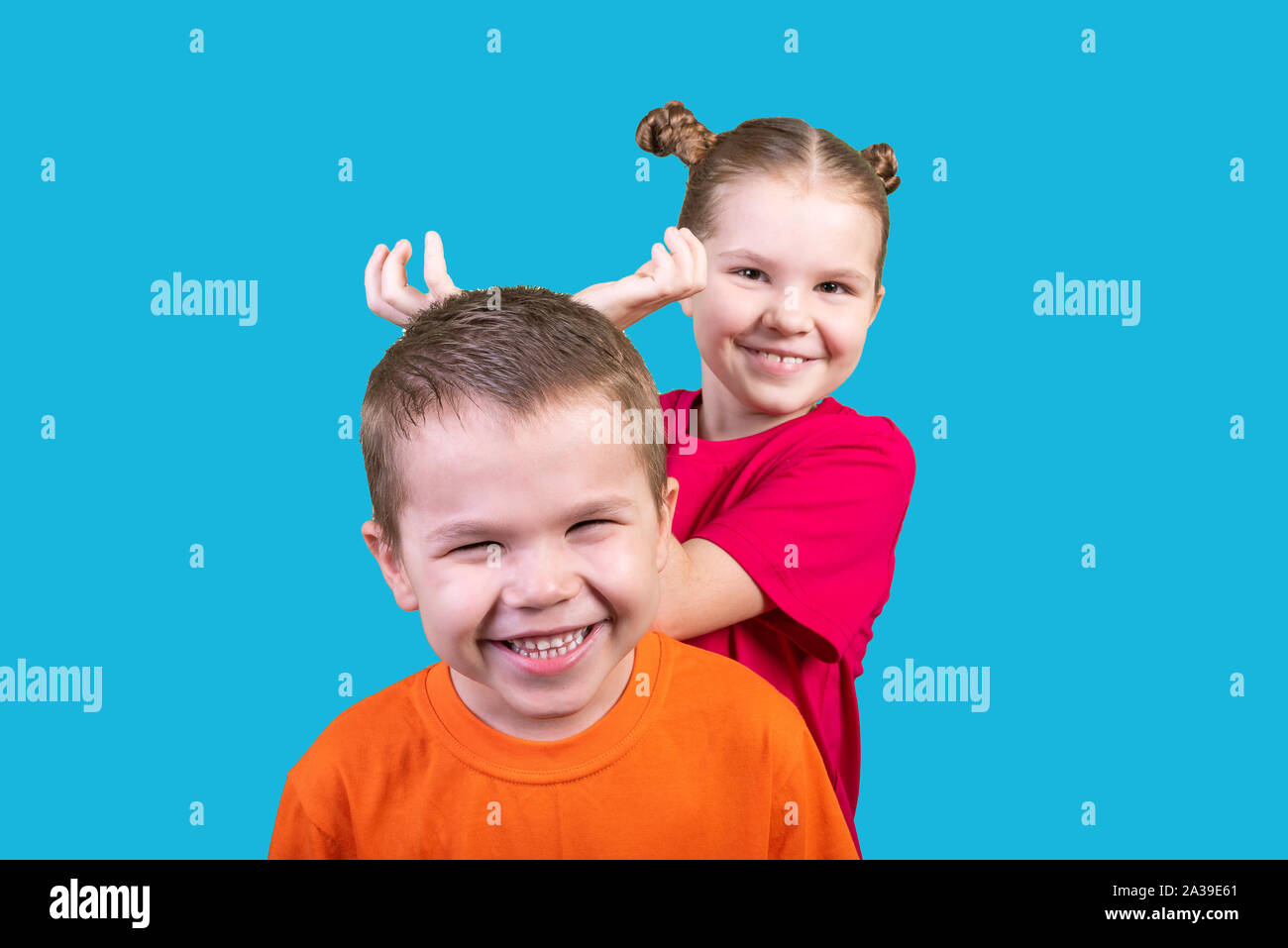 Little girl puts horns to a boy isolated on a blue background Stock ...