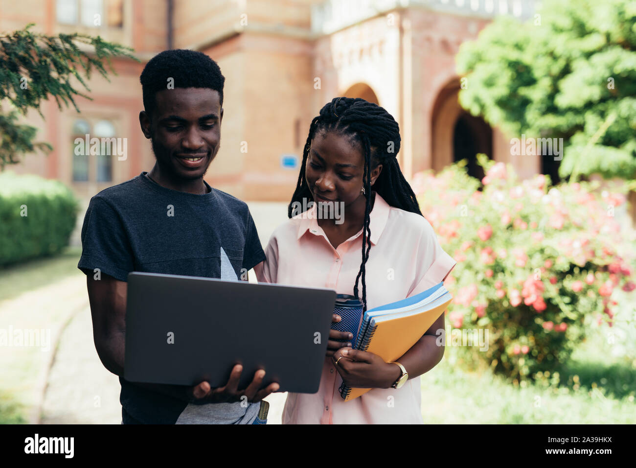 Two young students with laptop standing in campus yard Stock Photo - Alamy