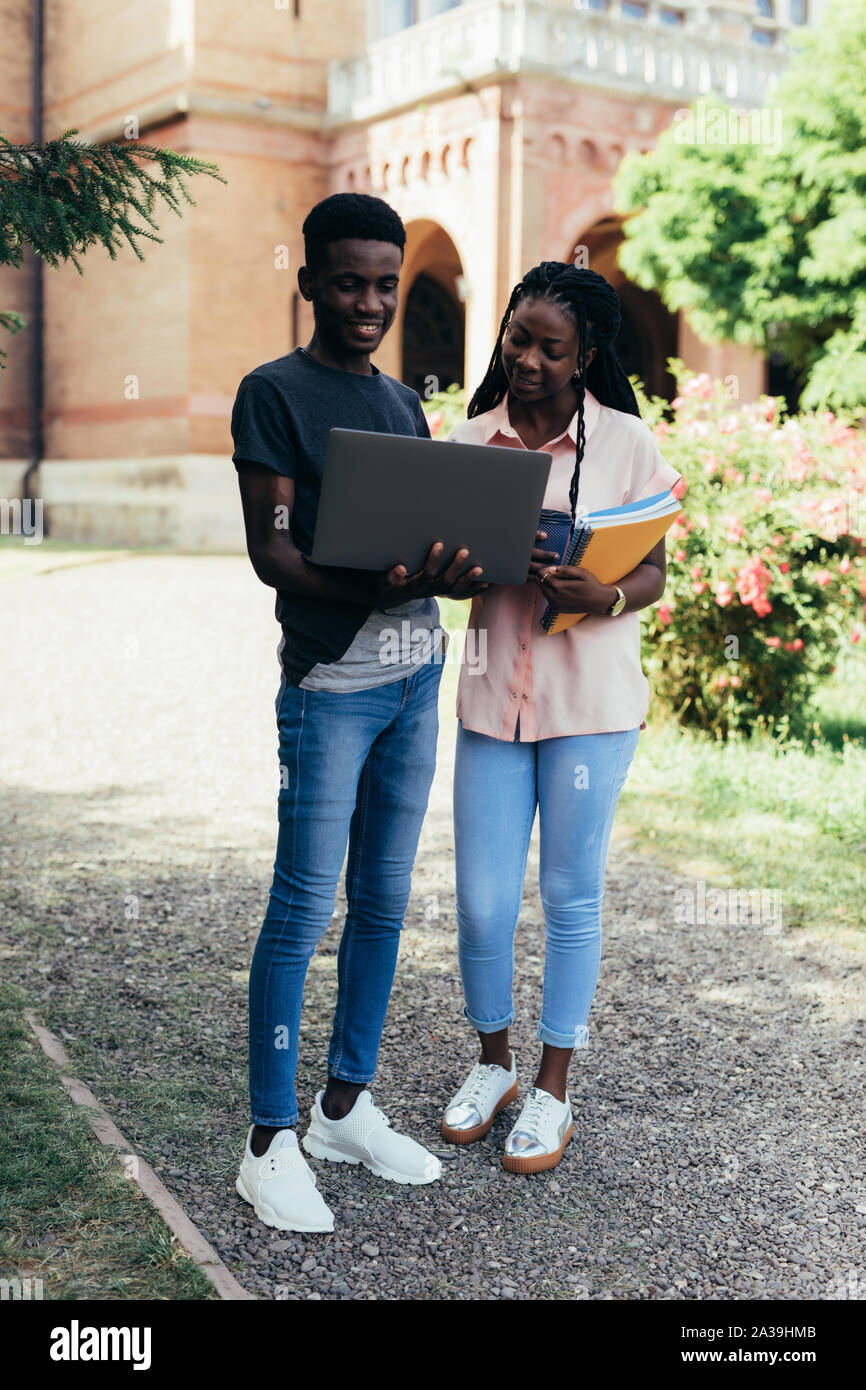 Two young students with laptop standing in campus yard Stock Photo - Alamy