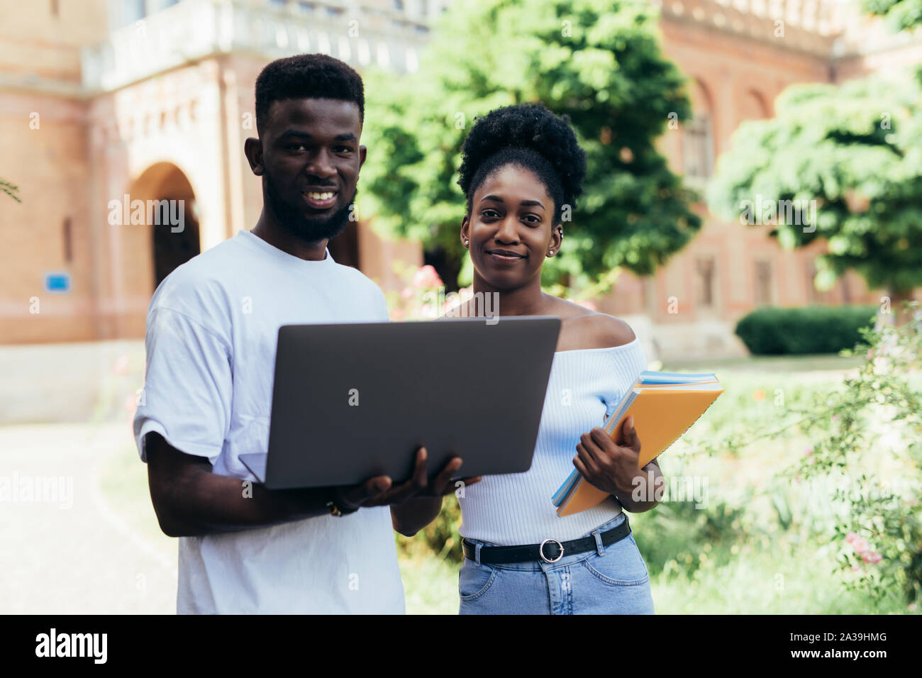 Two young students with laptop standing in campus yard Stock Photo - Alamy