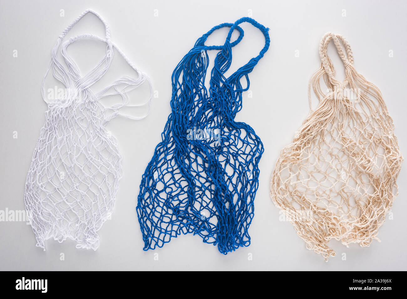 top view of eco friendly white, blue and beige string bags isolated on ...