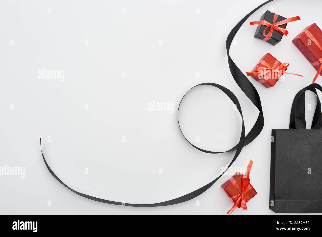 top view of black shopping bag, ribbon and red gift boxes on white ...