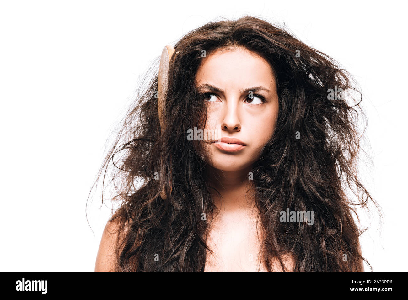 confused brunette woman with hairbrush in unruly curly hair isolated on ...
