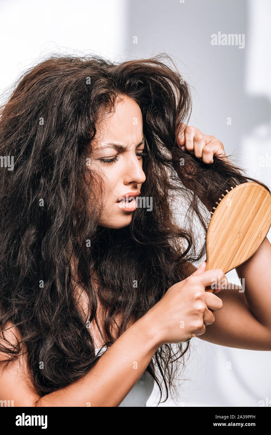 confused brunette woman styling unruly curly hair with hairbrush Stock ...