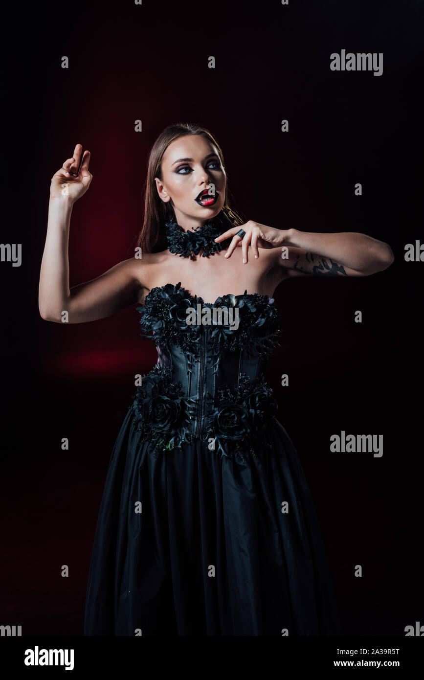 scary vampire girl with fangs in black gothic dress on black background ...