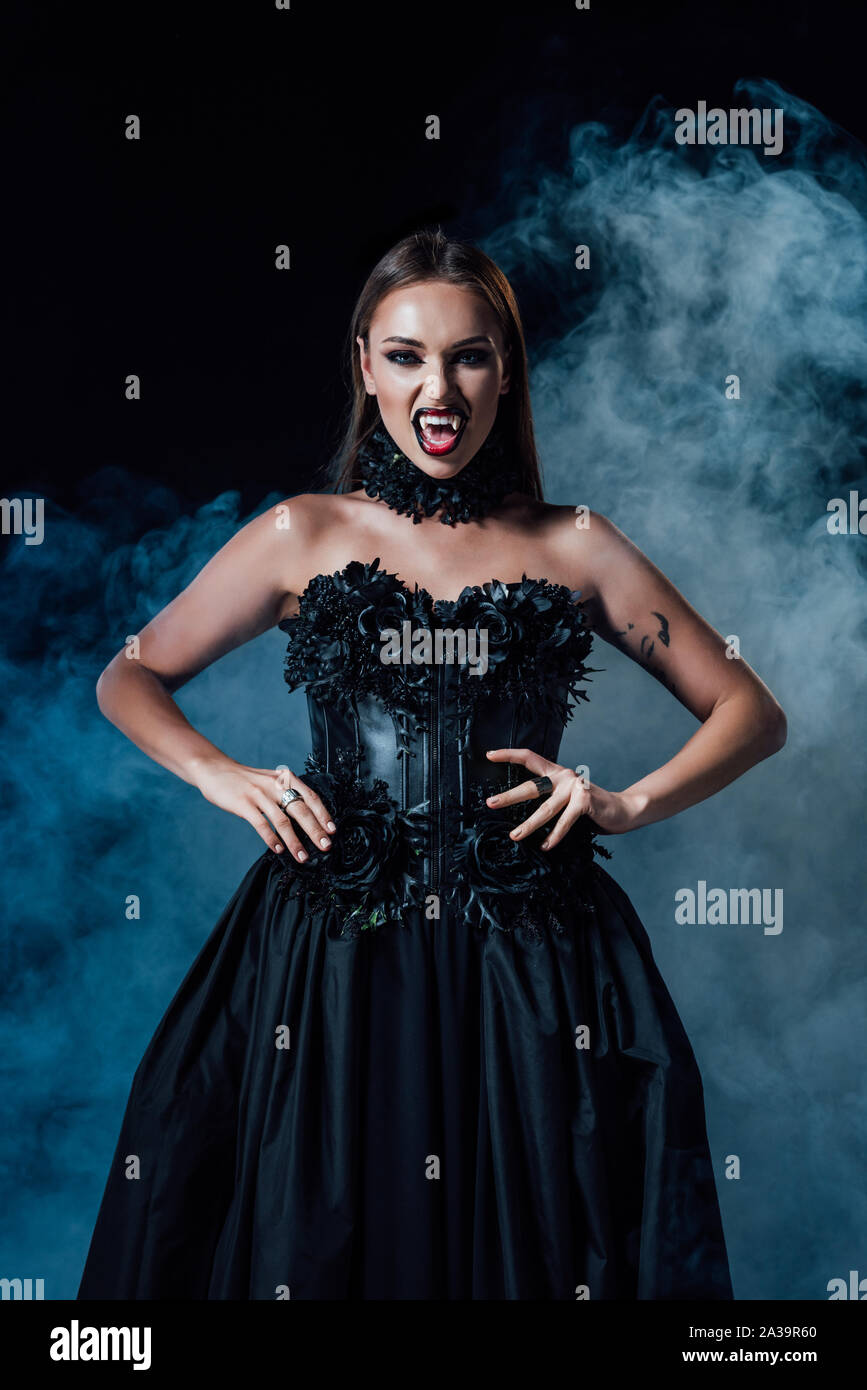 scary vampire girl with fangs in black gothic dress on black background ...