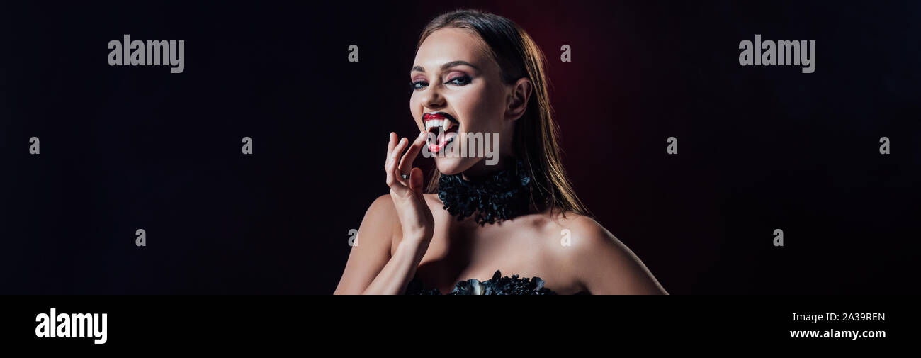 panoramic shot of scary vampire girl showing fangs in black gothic ...