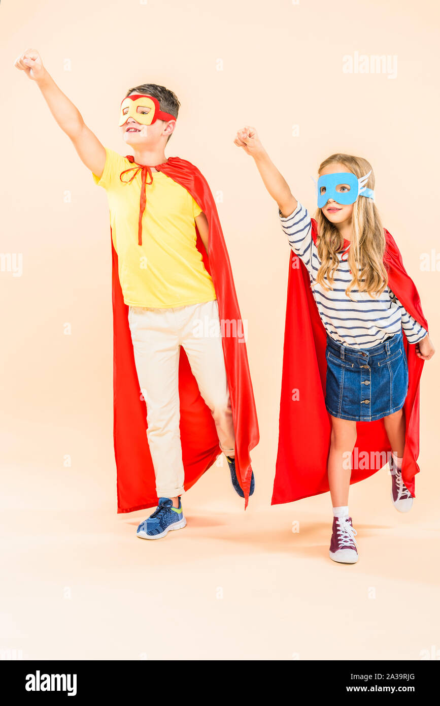 full length view of two smiling kids in masks and red cloaks holding ...