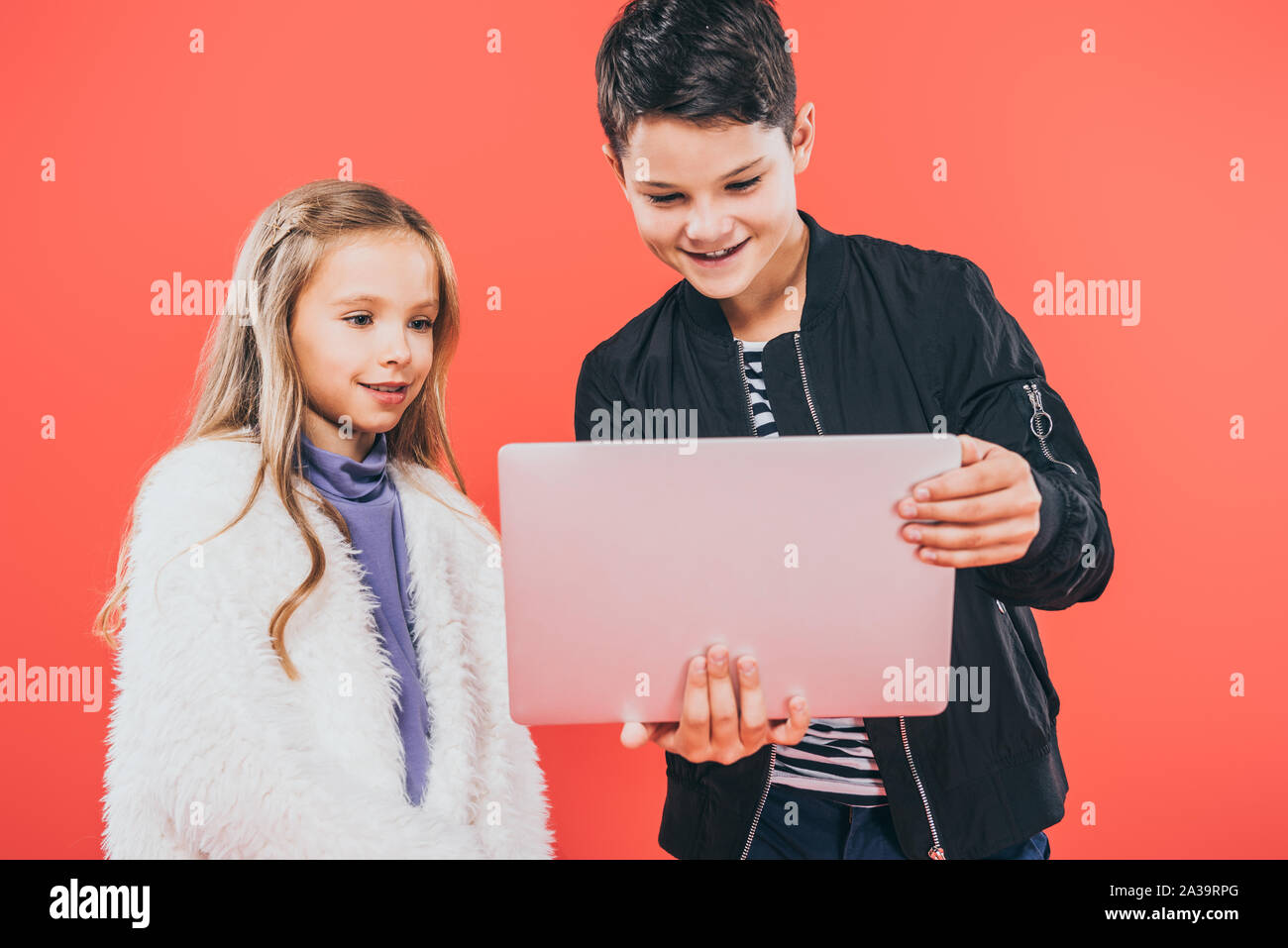 two smiling kids using laptop isolated on red Stock Photo - Alamy