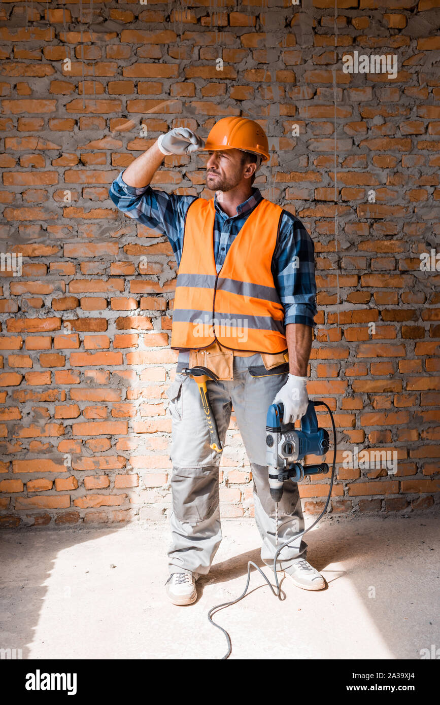 handsome bearded man holding hammer drill while touching helmet Stock ...