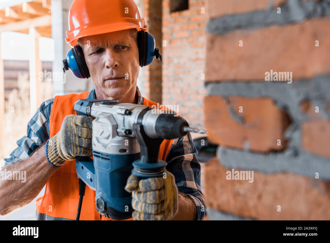 selective focus of mature man holding hammer drill near brick wall ...