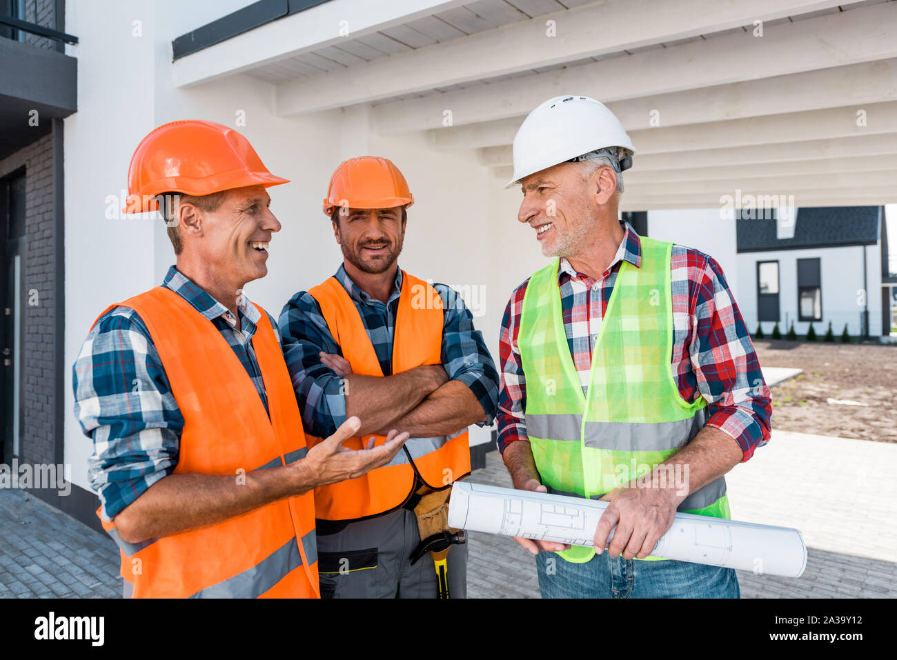 happy constructors in helmets standing near coworker with blueprint ...