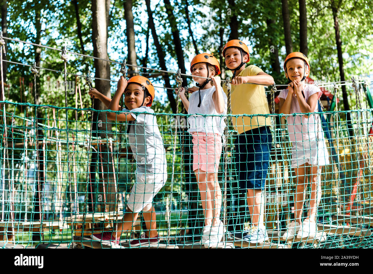 happy multicultural boys near friends in helmets in adventure park ...
