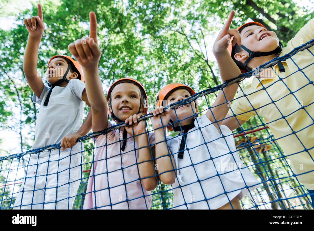 low angle view of smiling kids in orange helmets near multicultural ...