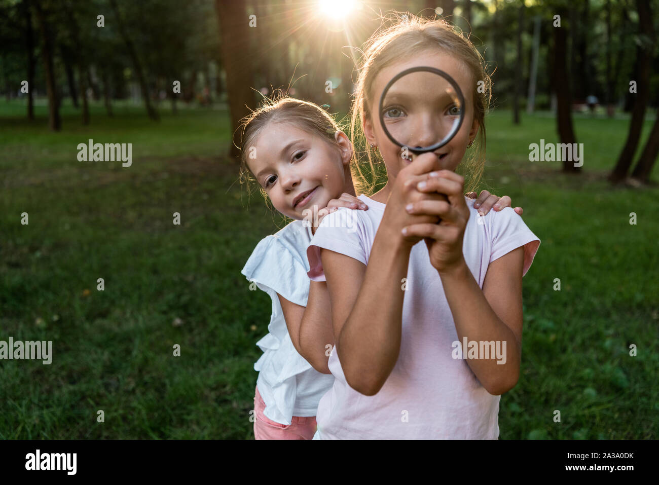happy kid holding magnifier near face while standing with friend in ...