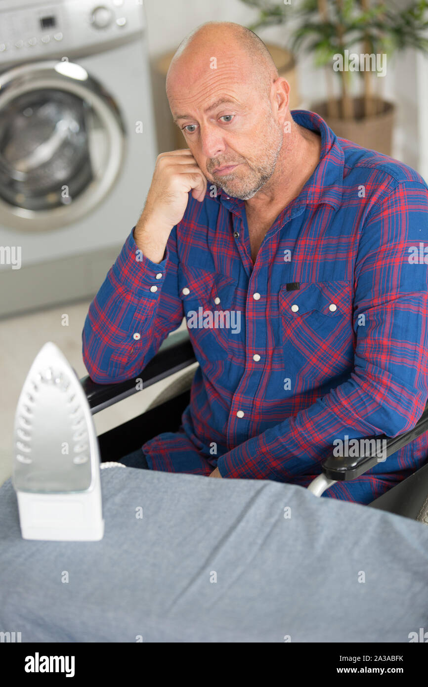 sad disabled man sitting in a wheelchair ironing shirt Stock Photo - Alamy