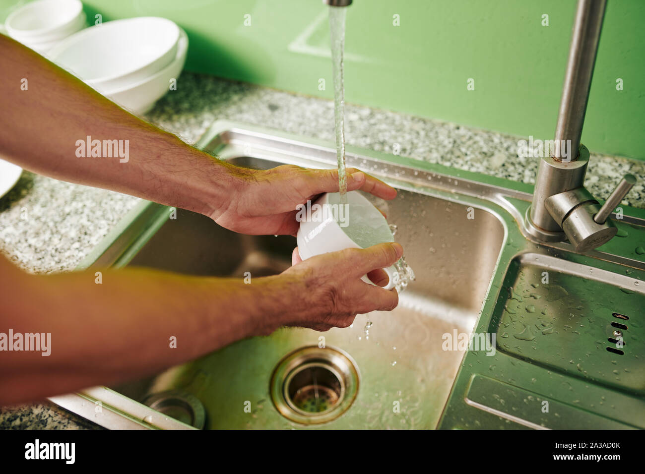 Hands of man washing dishes after dinner. He is rinsing coffee cup ...