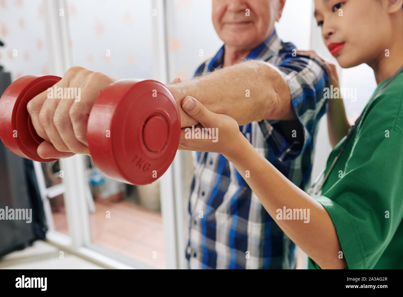 Medical nurse controlling senior patient lifting dumbbell when having ...