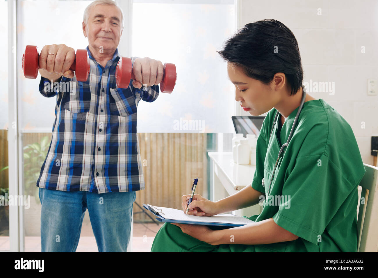 Smiling senior man doing exercises with dumbbells when nurse taking ...
