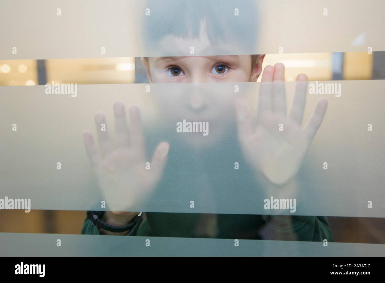 The child is looking through the glass. Boy peeps in frosted glass ...