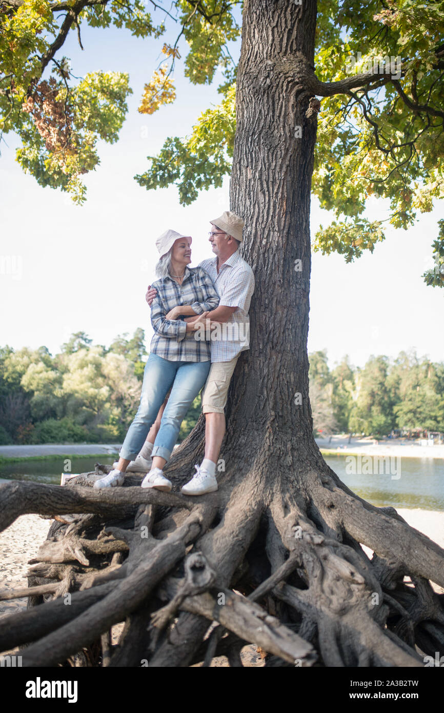 Couple of mature adults standing on roots of huge tree Stock Photo - Alamy