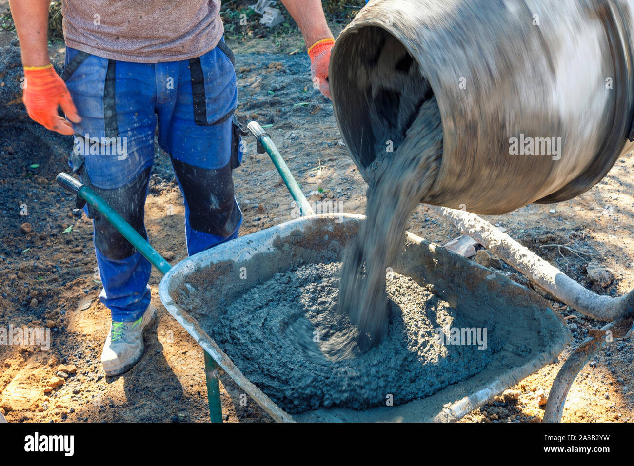 Builder pouring cement from a cement mixer into a wheelbarrow waiting ...