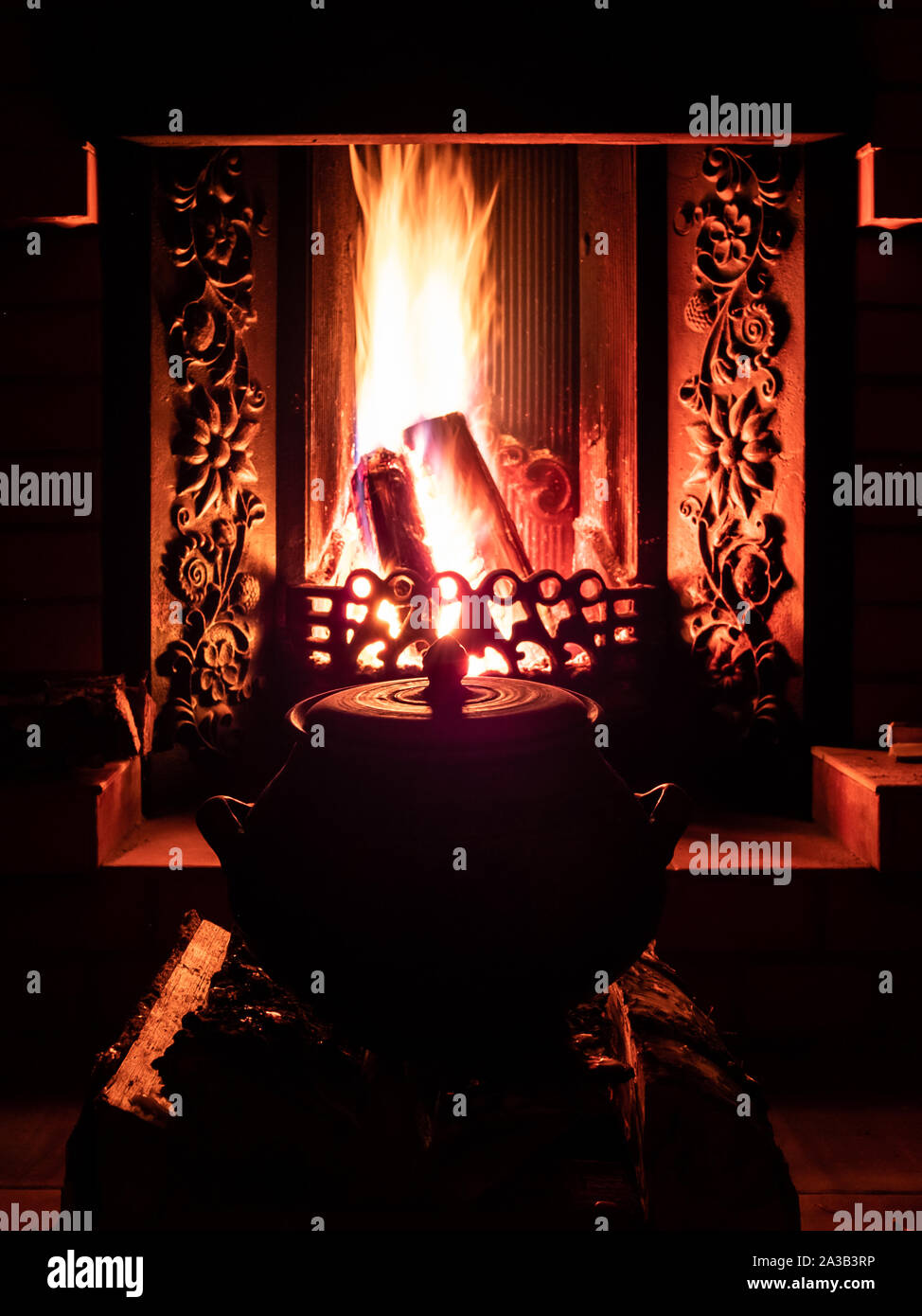 An old cauldron standing in the dark in front of the wood burning in ...