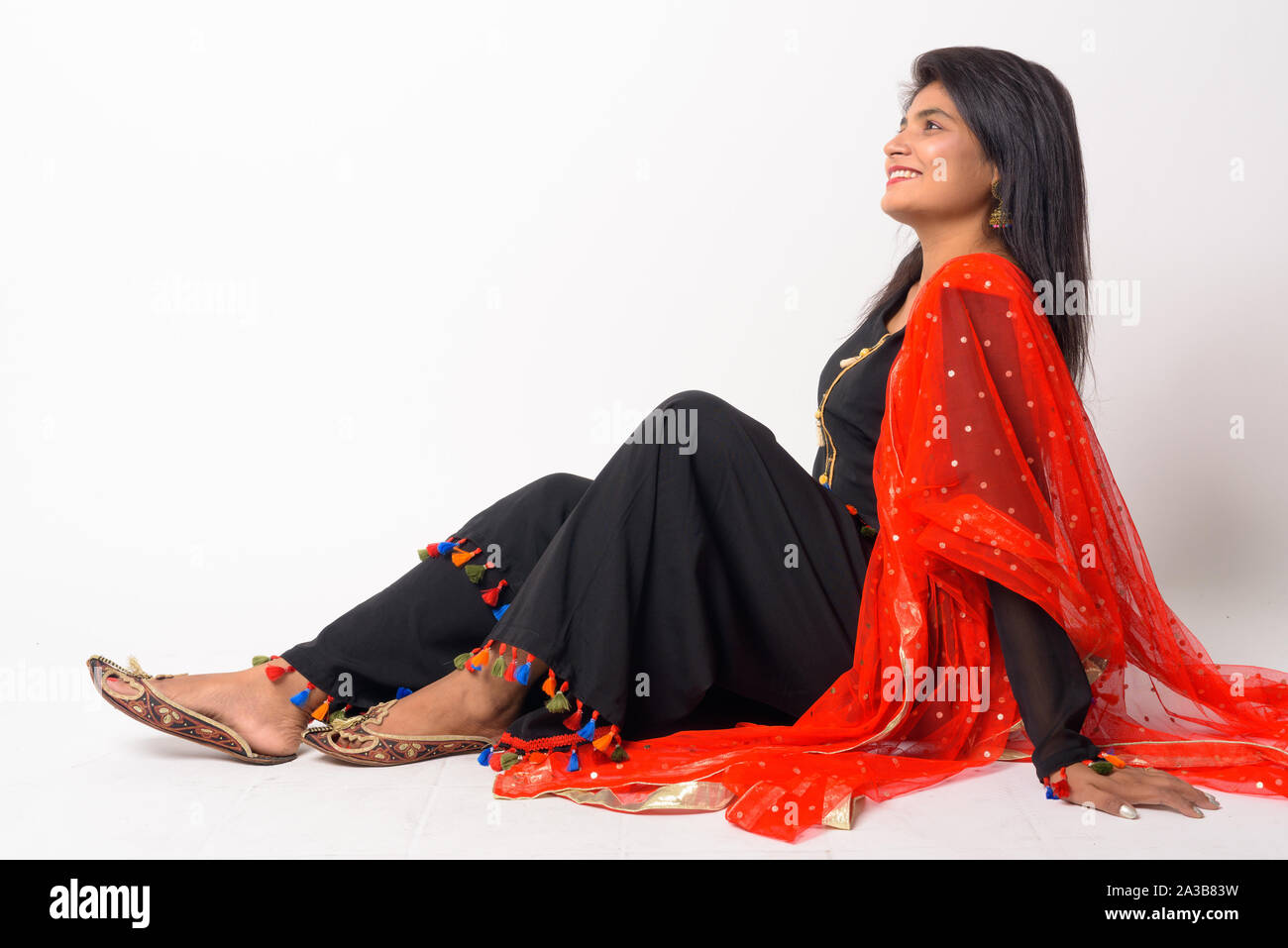 Full body shot of happy young Persian woman thinking while sitting on ...