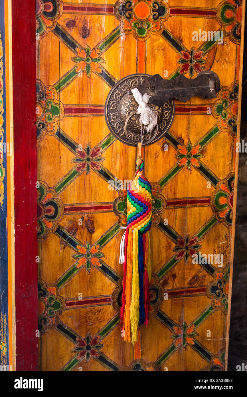 An ornately decorated old wooden door with a plaited Buddhist tassel in ...