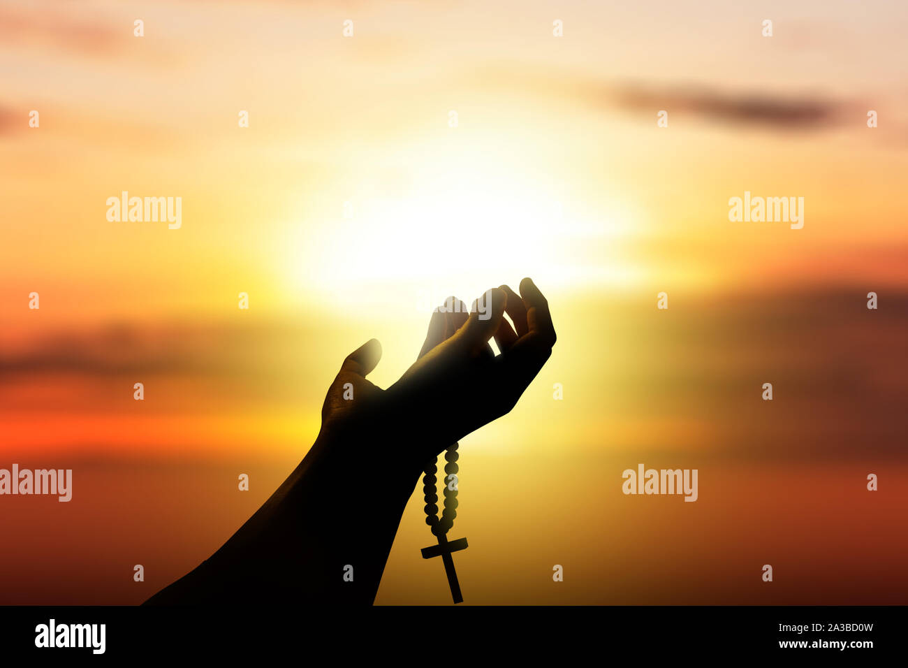 Human hands with rosary beads raised while praying to god with a sunset ...