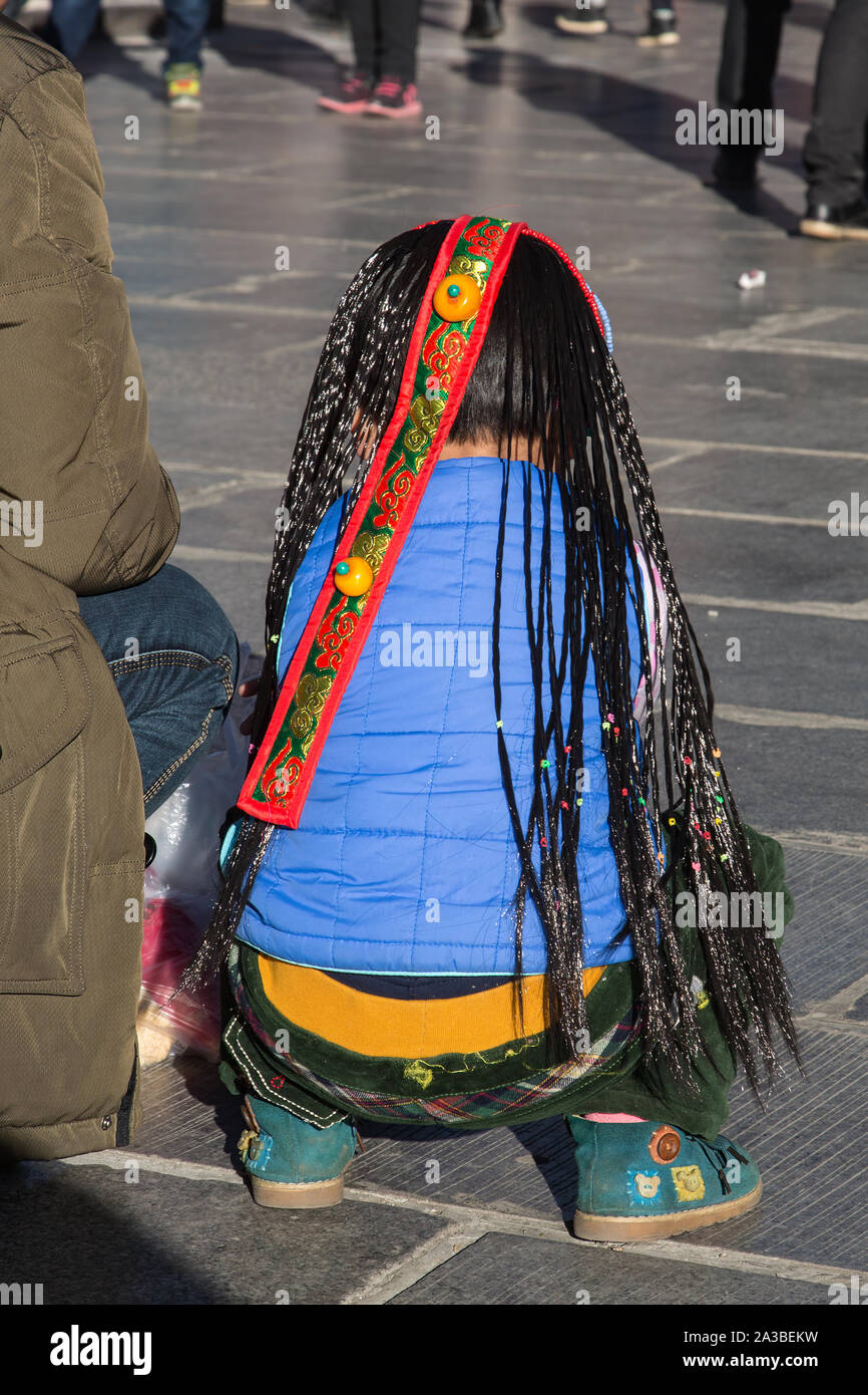 A young Tibetan girl wears a wig of Khamba-style braids and a red coral ...