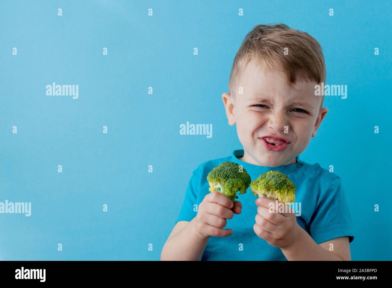 Little kid holding broccoli in his hands on blue background. Vegan and ...