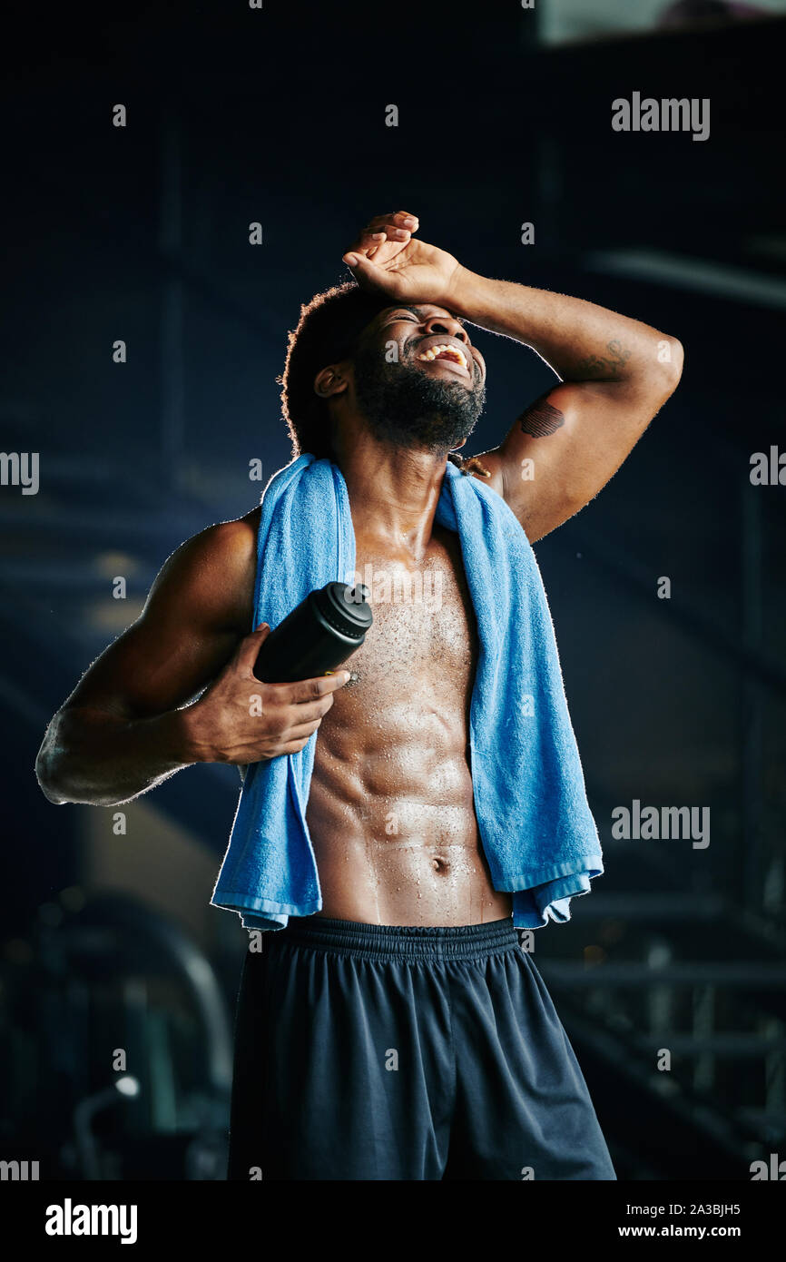 Sweaty shirtless athlete with bottle of water wiping forehead and ...