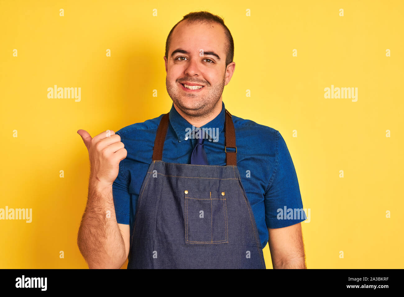 Young shopkeeper man wearing apron standing over isolated yellow ...