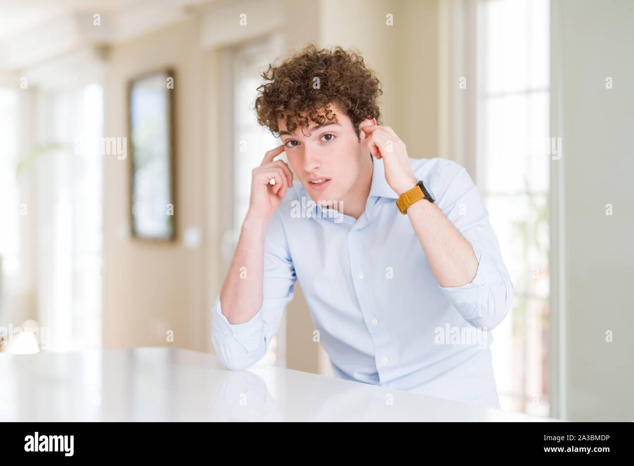 Young business man with curly read head covering ears with fingers with ...
