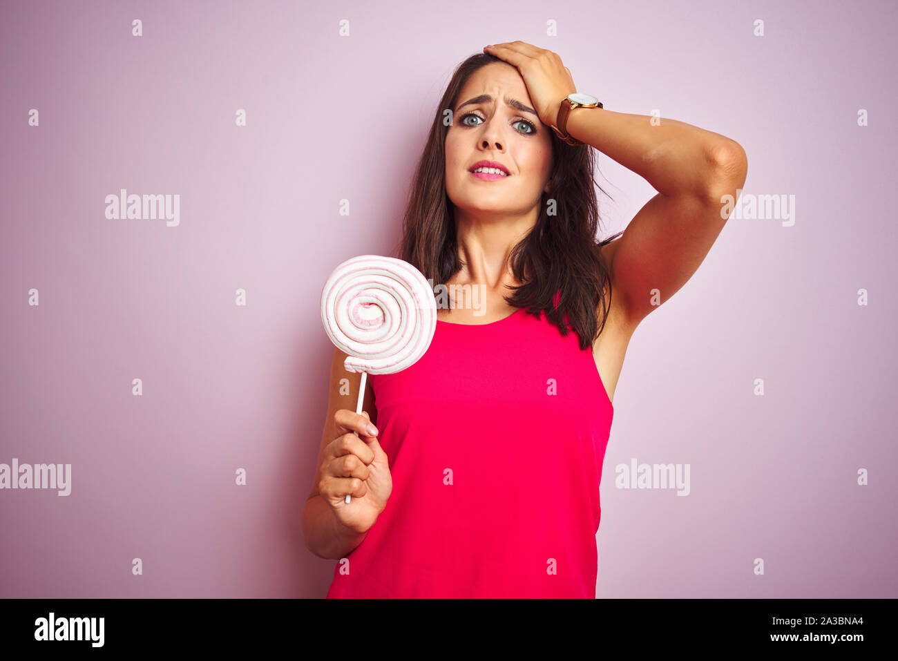 Young beautiful woman eating sweet candy over pink isolated background ...