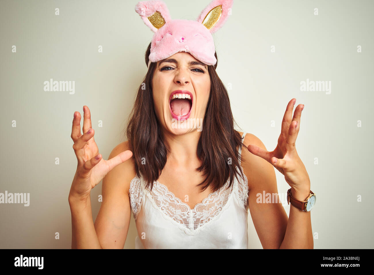 Young beautiful woman wearing pajama and mask standing over white ...