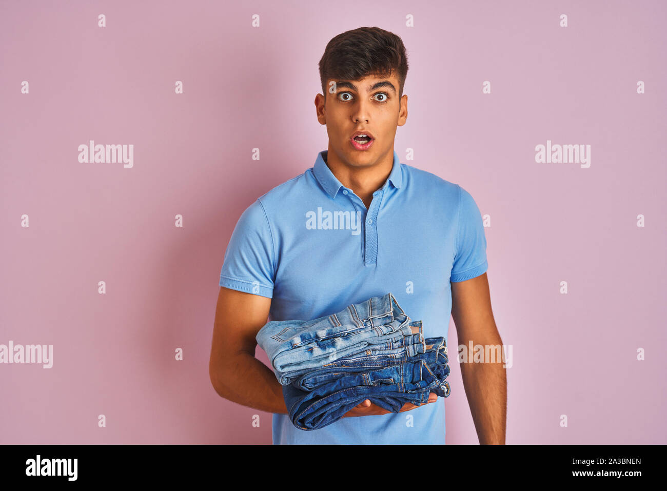 Young indian shopkeeper man holding folded jeans standing over isolated ...