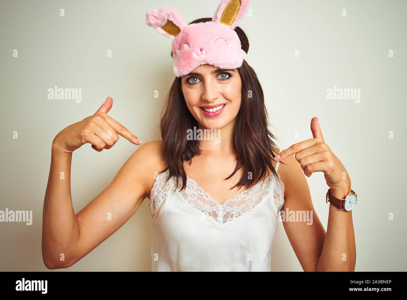 Young beautiful woman wearing pajama and mask standing over white ...
