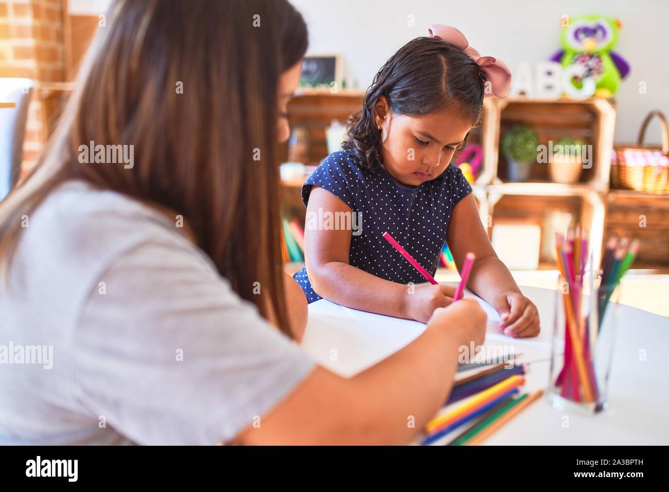 Beautiful teacher and toddler girl drawing draw using colored pencils ...