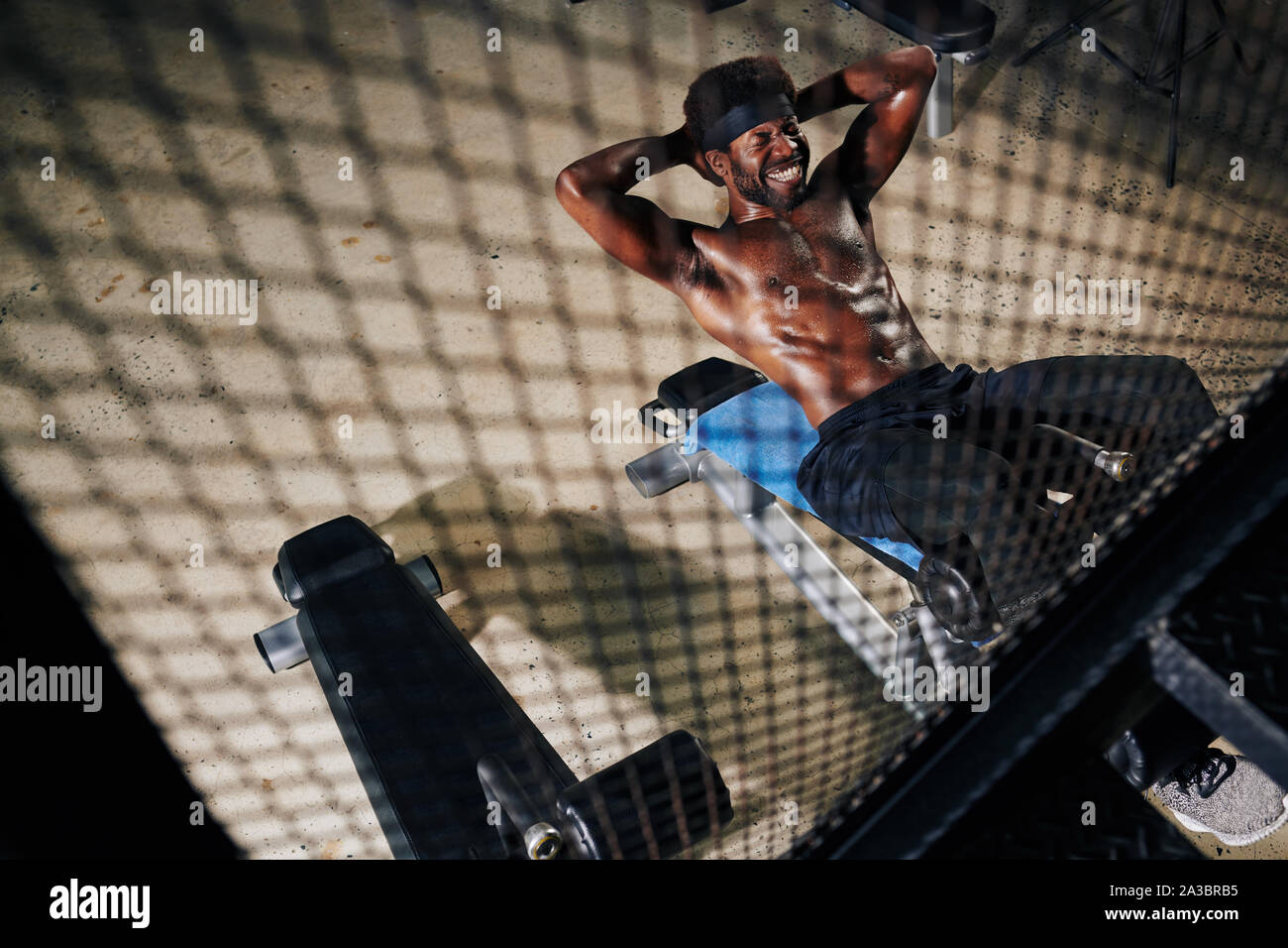 Sweaty Black young man working hard when doing sit-ups on gym bench ...