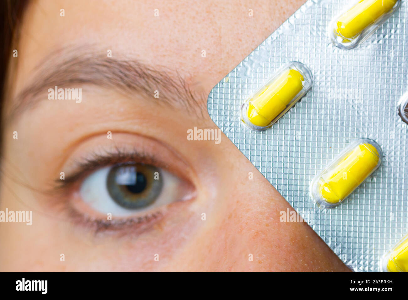 Woman shows yellow pill. Close up of woman eye Stock Photo - Alamy