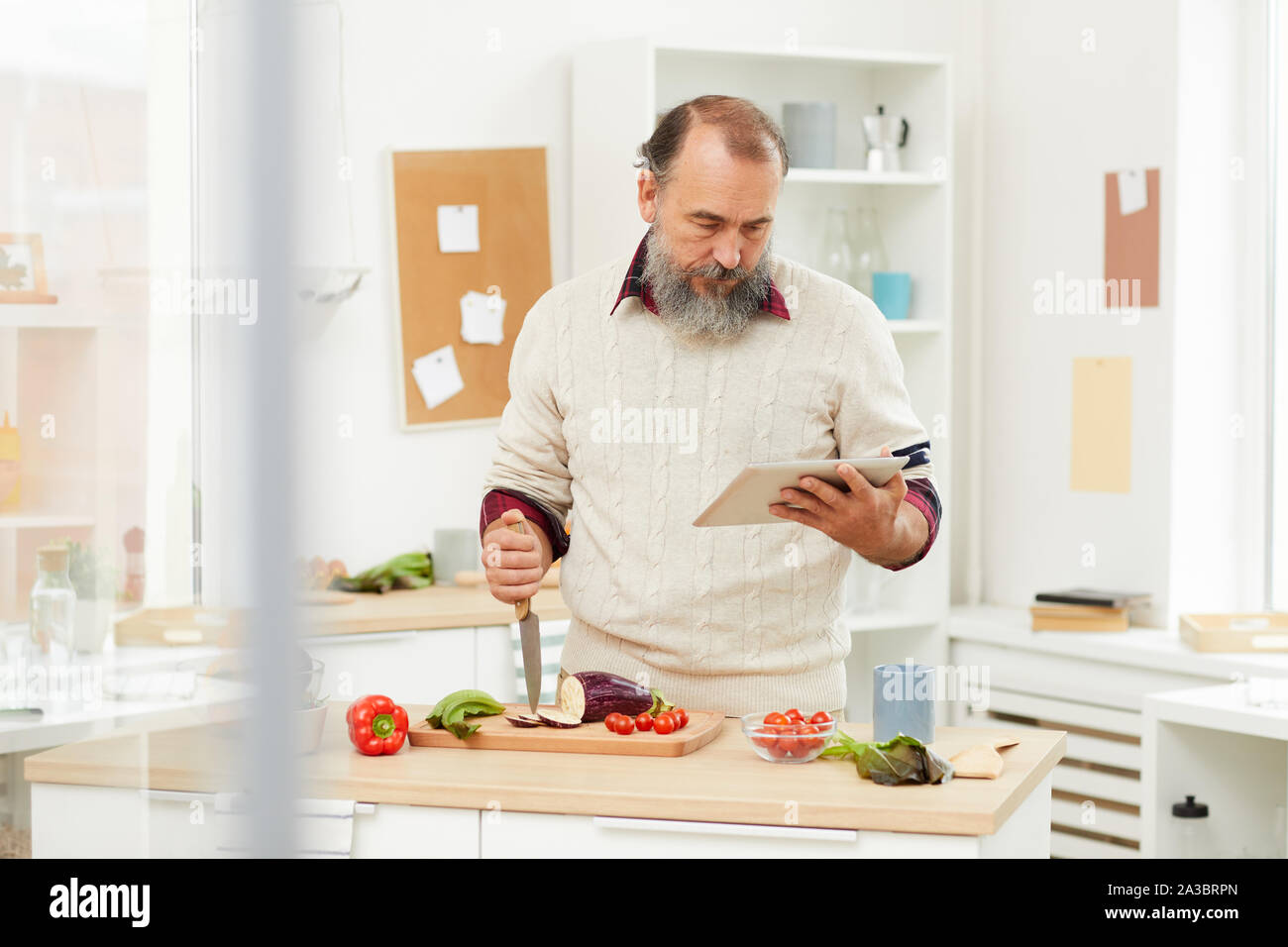 Waist up portrait of bearded senior man looking up recipe via digital ...
